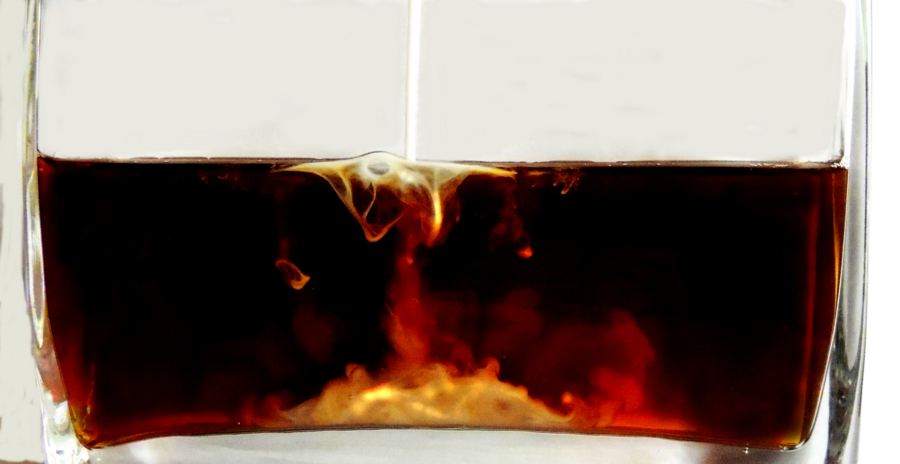 A stream of creamer entering coffee splits_ some remains on the surface ...